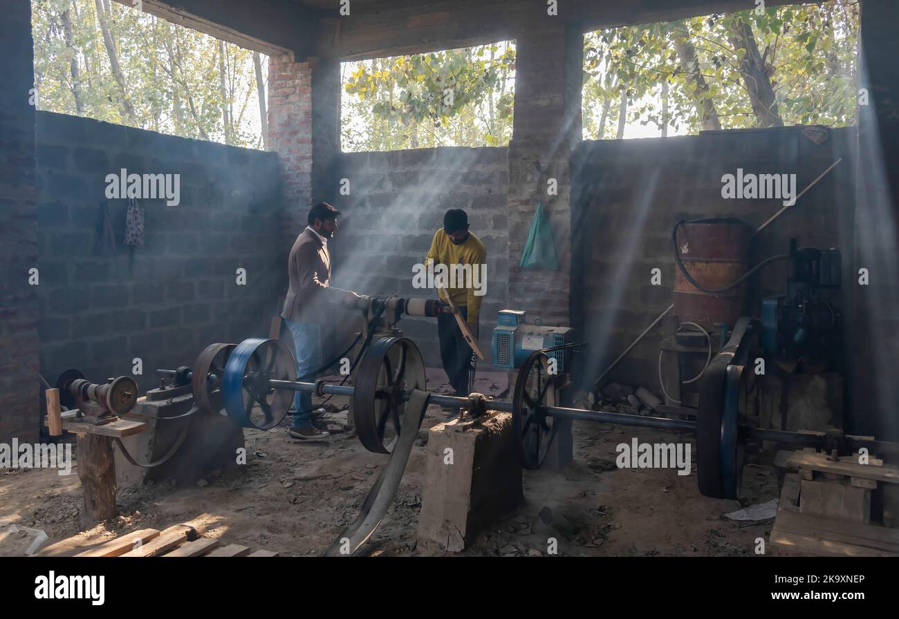 A worker shapes willow on a machine to produce bats at a factory in ...