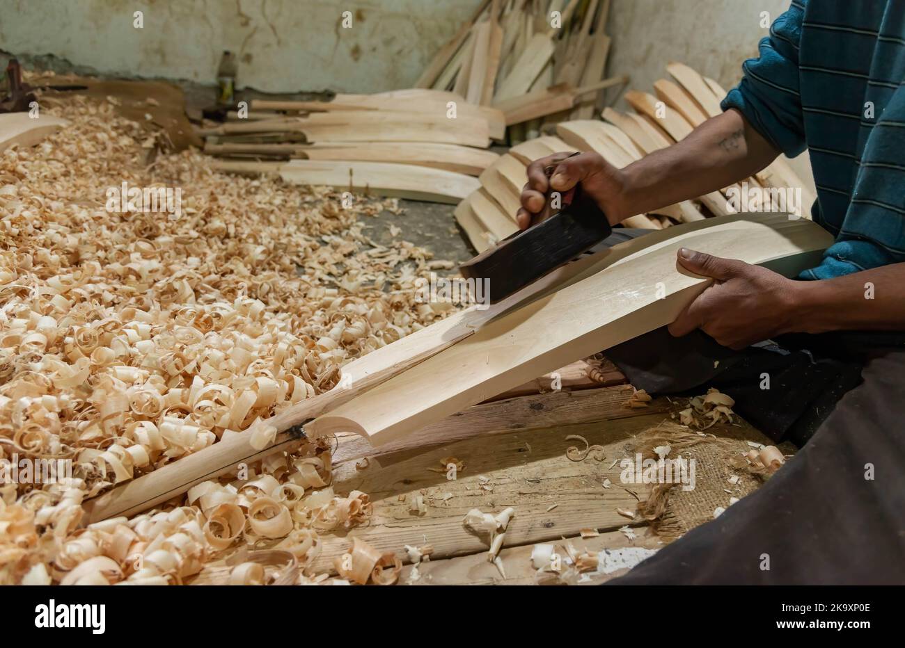 A worker shapes a willow with a woodworking tool to produce cricket bat ...