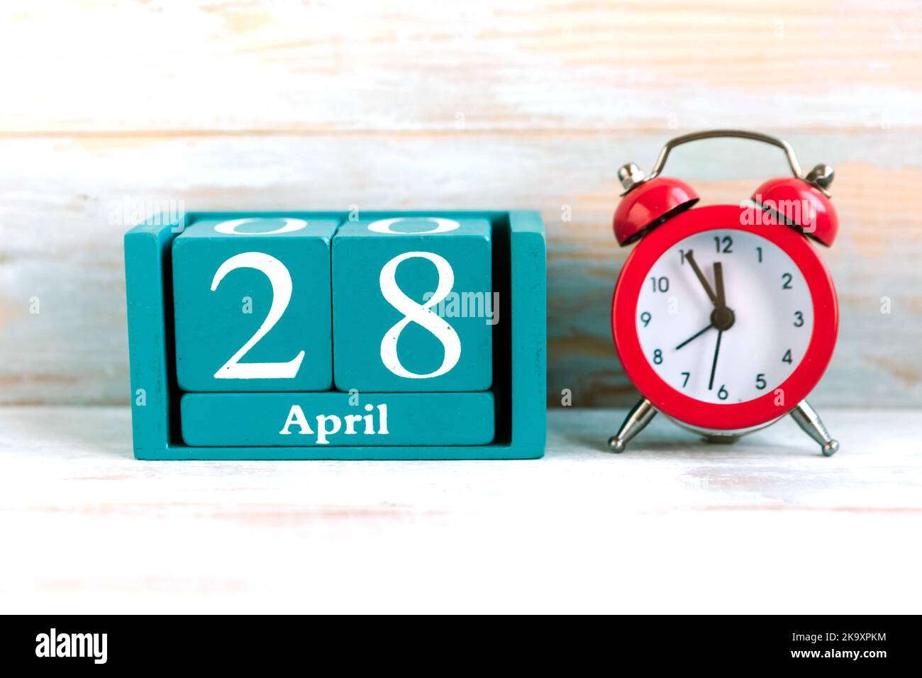 April 28. Blue cube calendar with month and date and red alarm clock on wooden background Stock ...