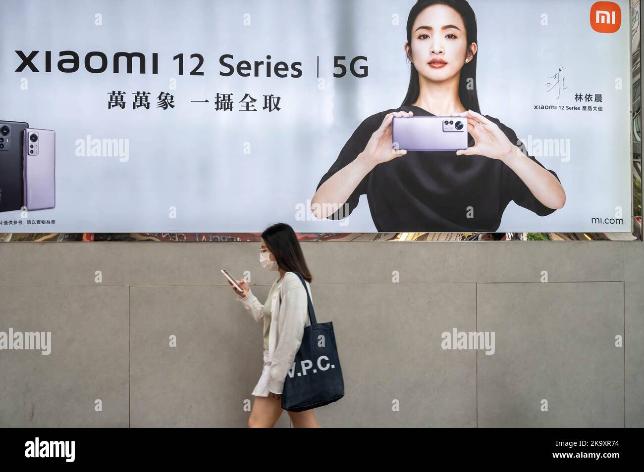 A pedestrian using a phone walks past the Xiaomi Mi 12 5G smartphone ...