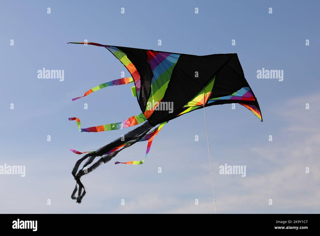 Large black kite with multicolored rainbow stripes flies high in the ...