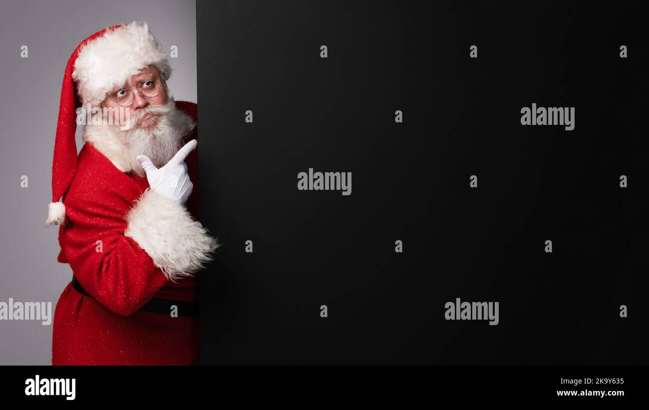 Happy smiling Santa Claus pointing with open hand palm at black banner ...