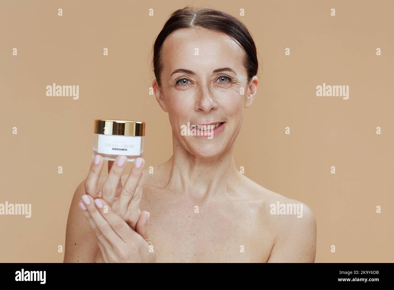 Portrait of modern female with facial cream jar on beige background ...