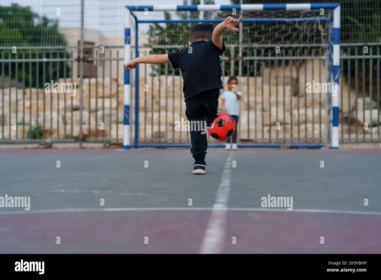 Back view of boy kicking soccer ball. Young girl soccer goalkeeper ...