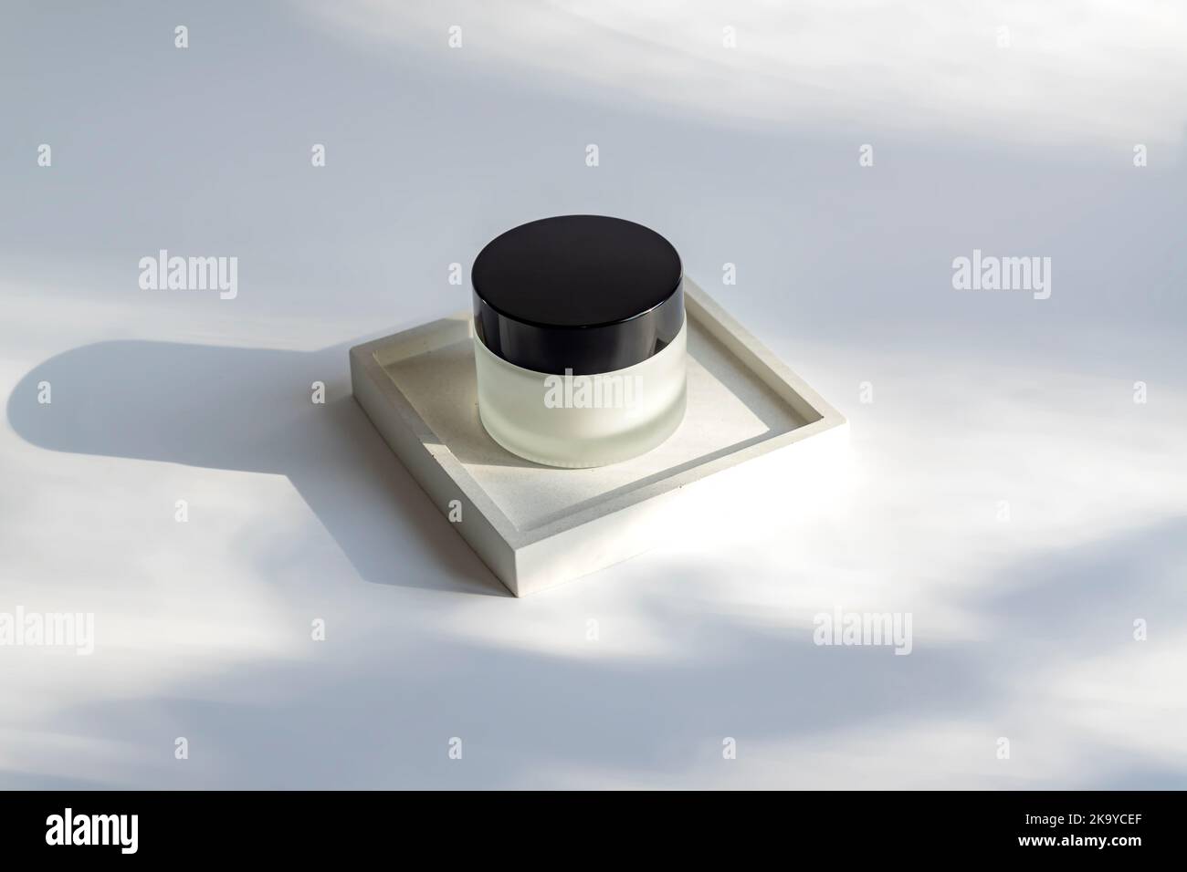 A jar of cream on concrete tray on a white background with harsh ...