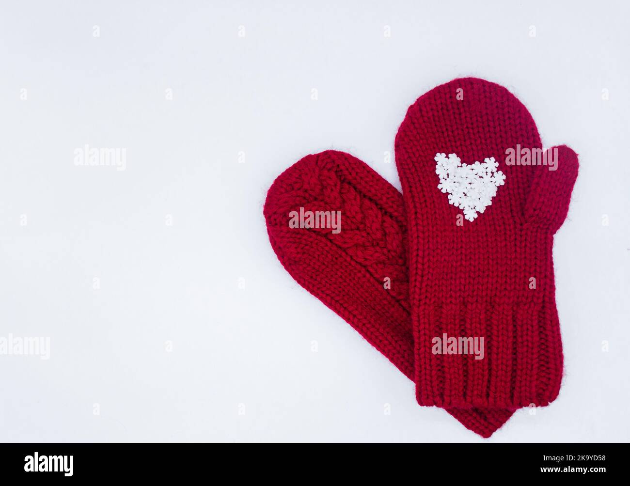 Two knitted red mittens lie one each other with white snowflakes in the ...