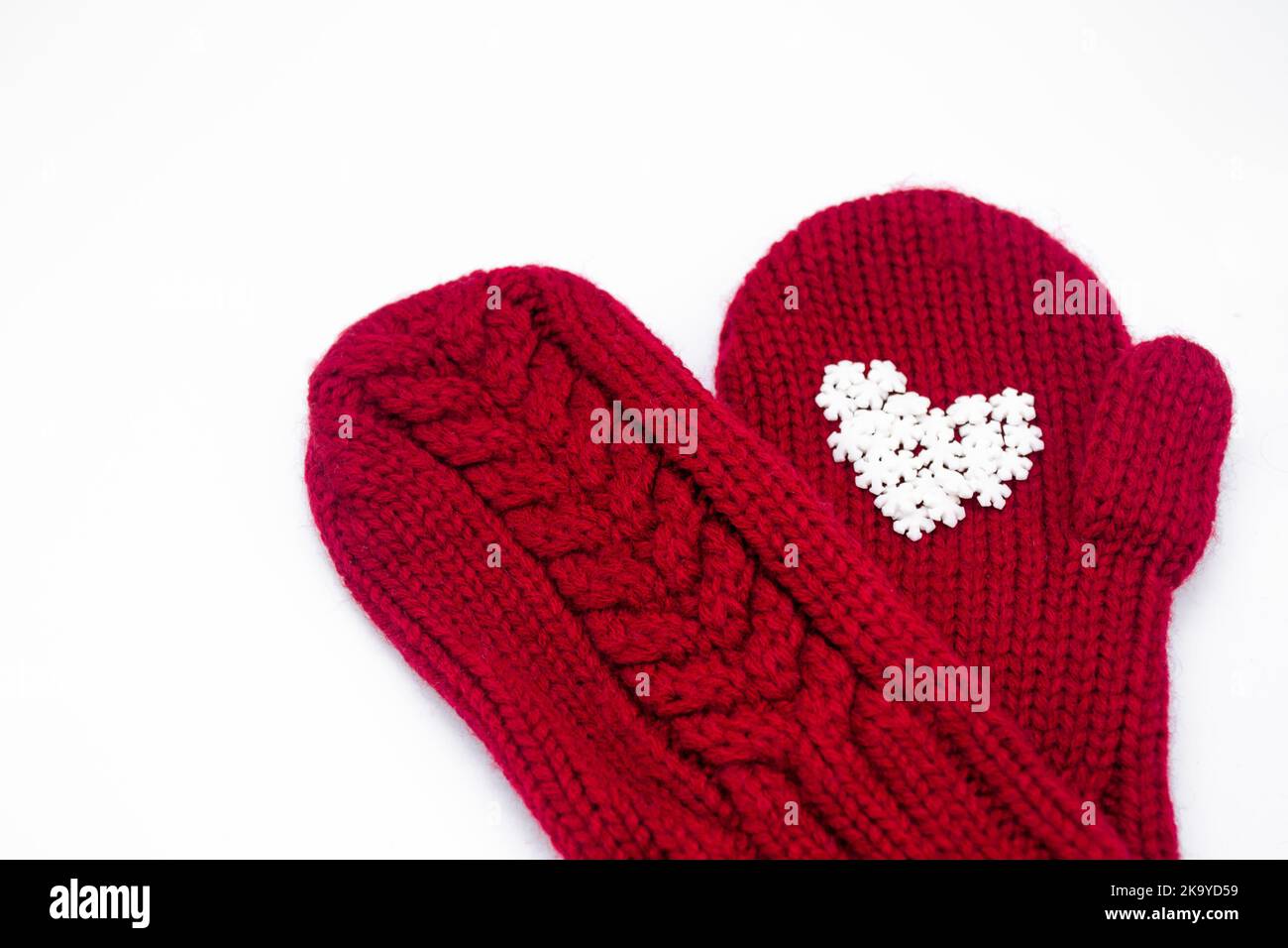 Two knitted red mittens lie one each other with white snowflakes in the ...