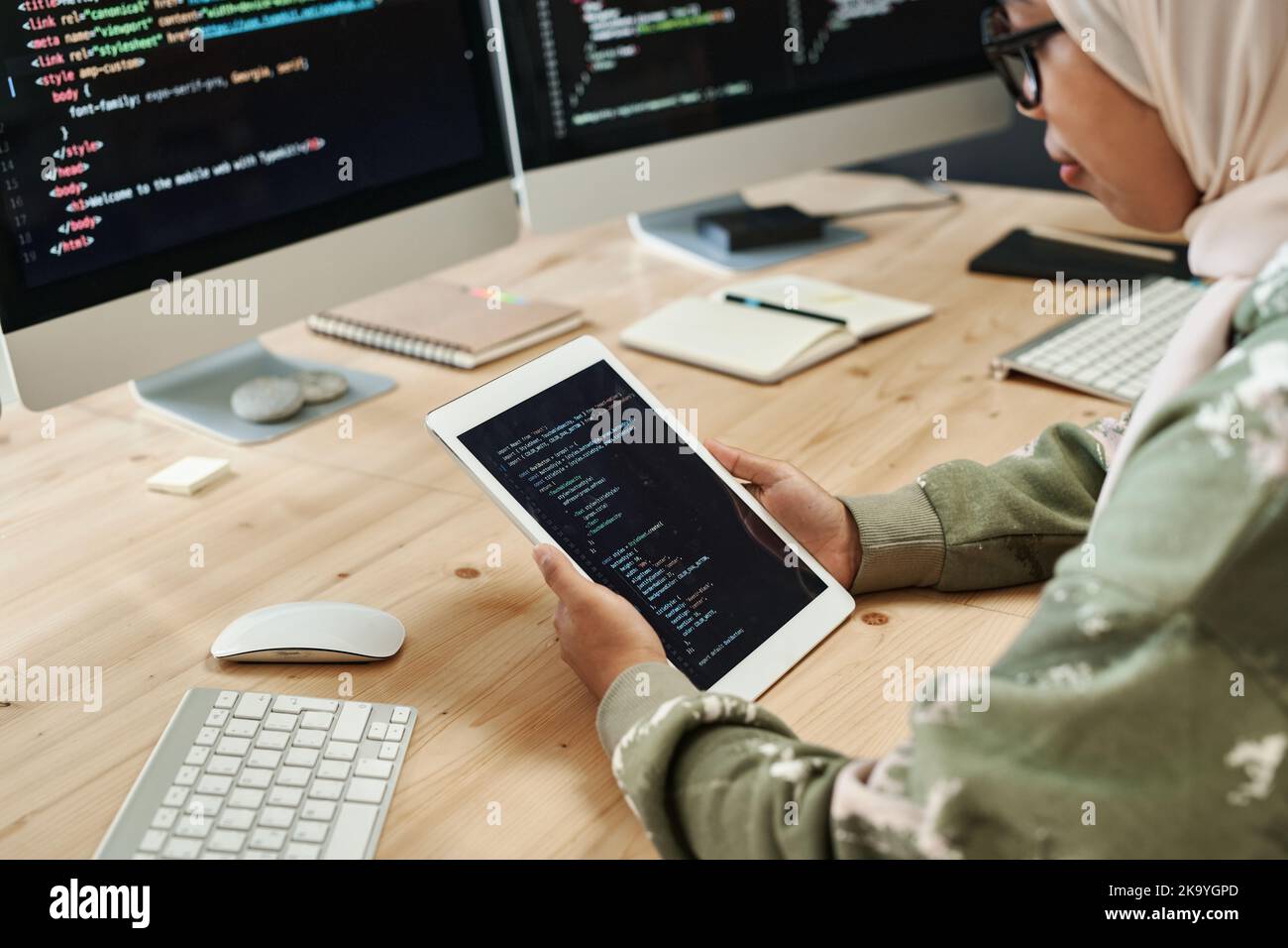 Close-up of young Muslim female programmer looking through coded data on tablet screen while ...