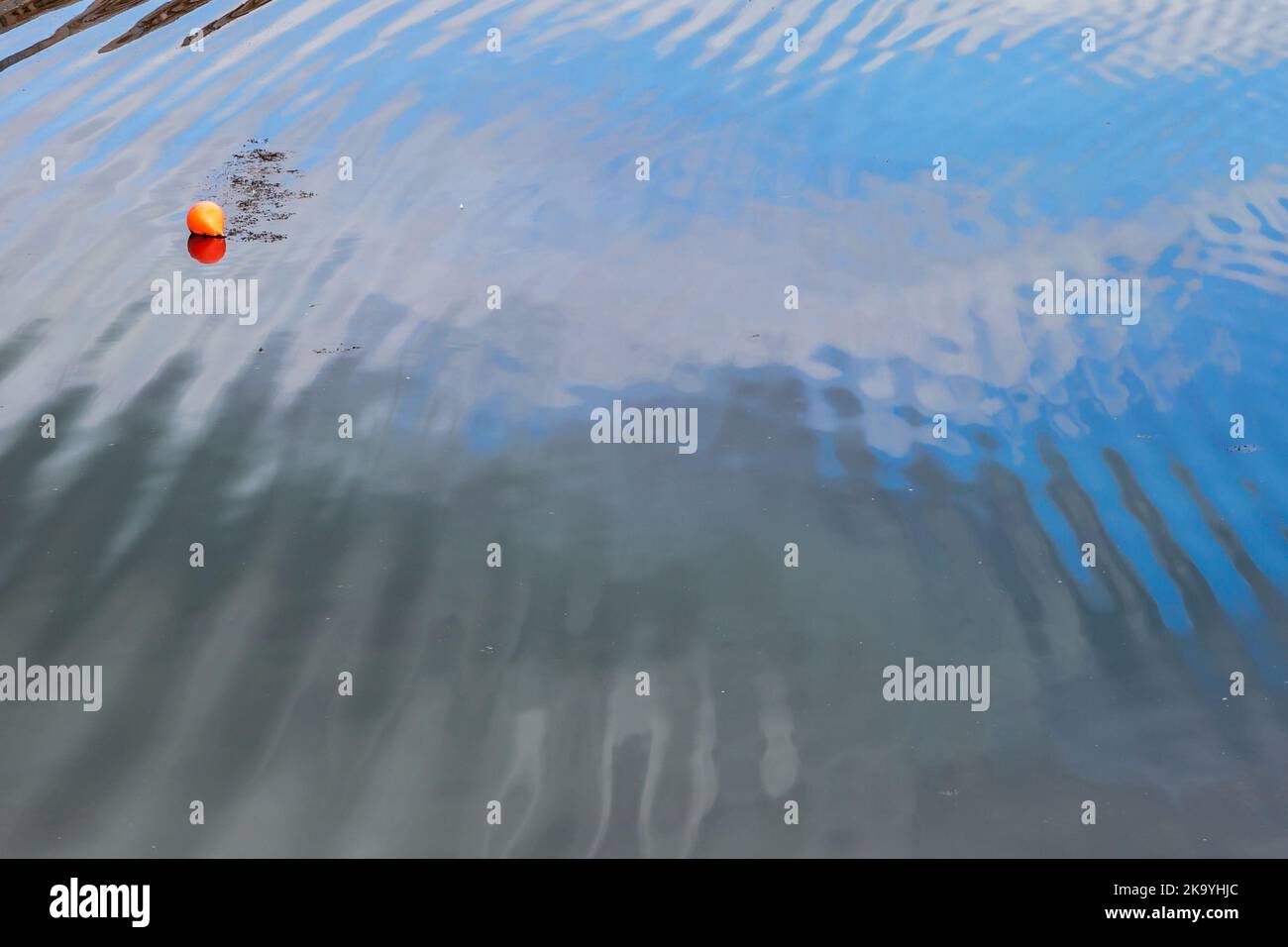 Looking down at water in a harbour with a buoy floating on the surface ...