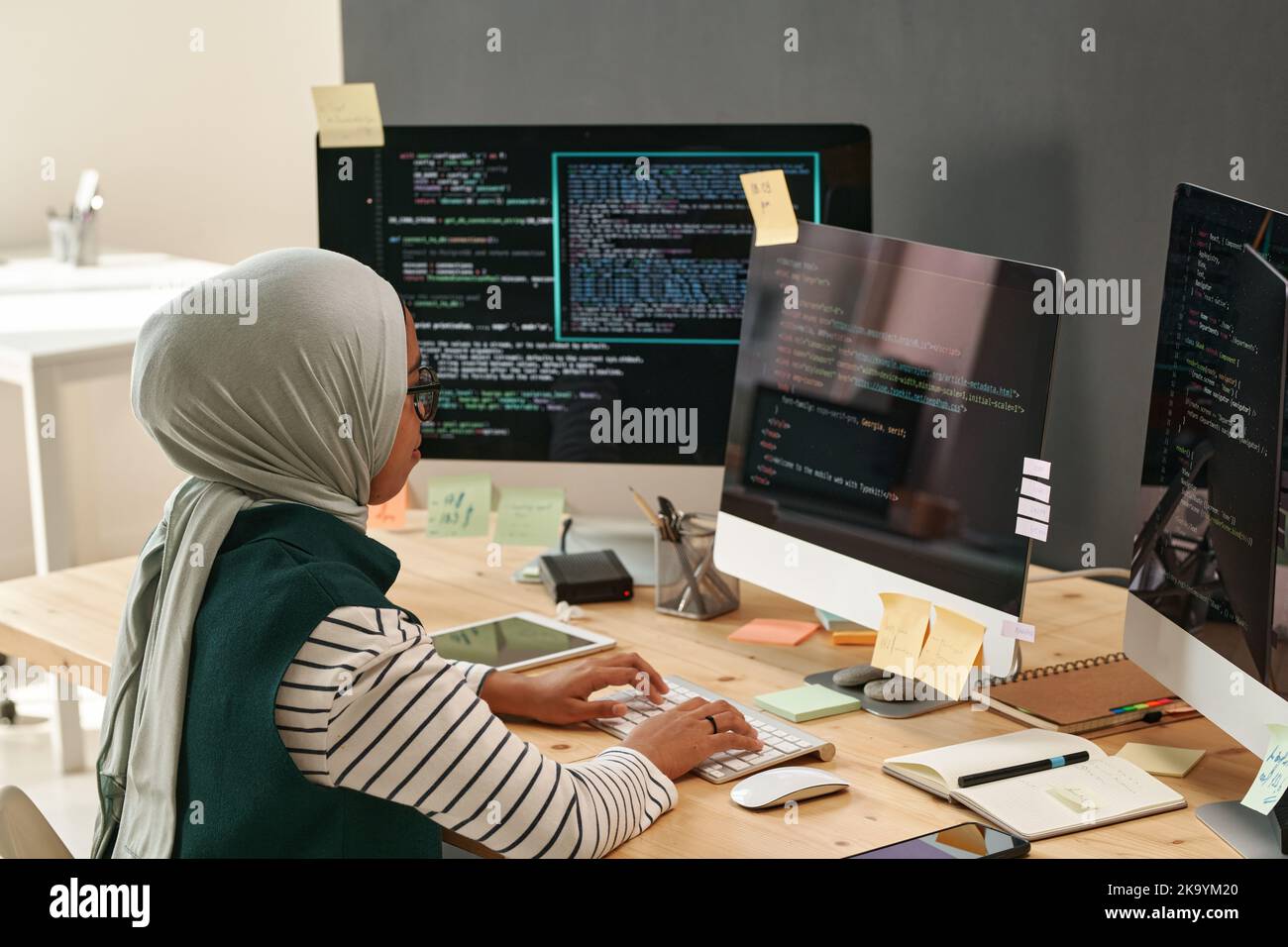 Young woman in hijab typing on computer keyboard while sitting by ...