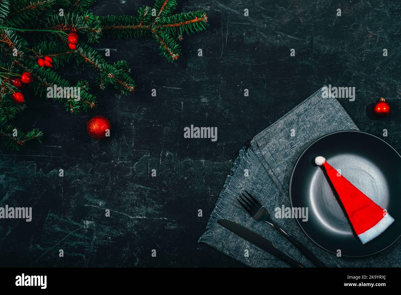 Table setting with black plate, fork, knife, santa hat, fir branch and ...