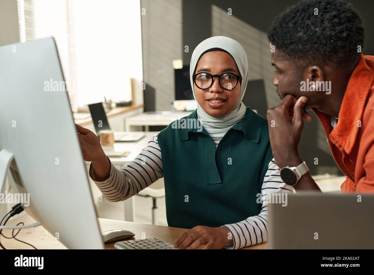 Young confident Muslim woman in hijab pointing at computer screen and ...