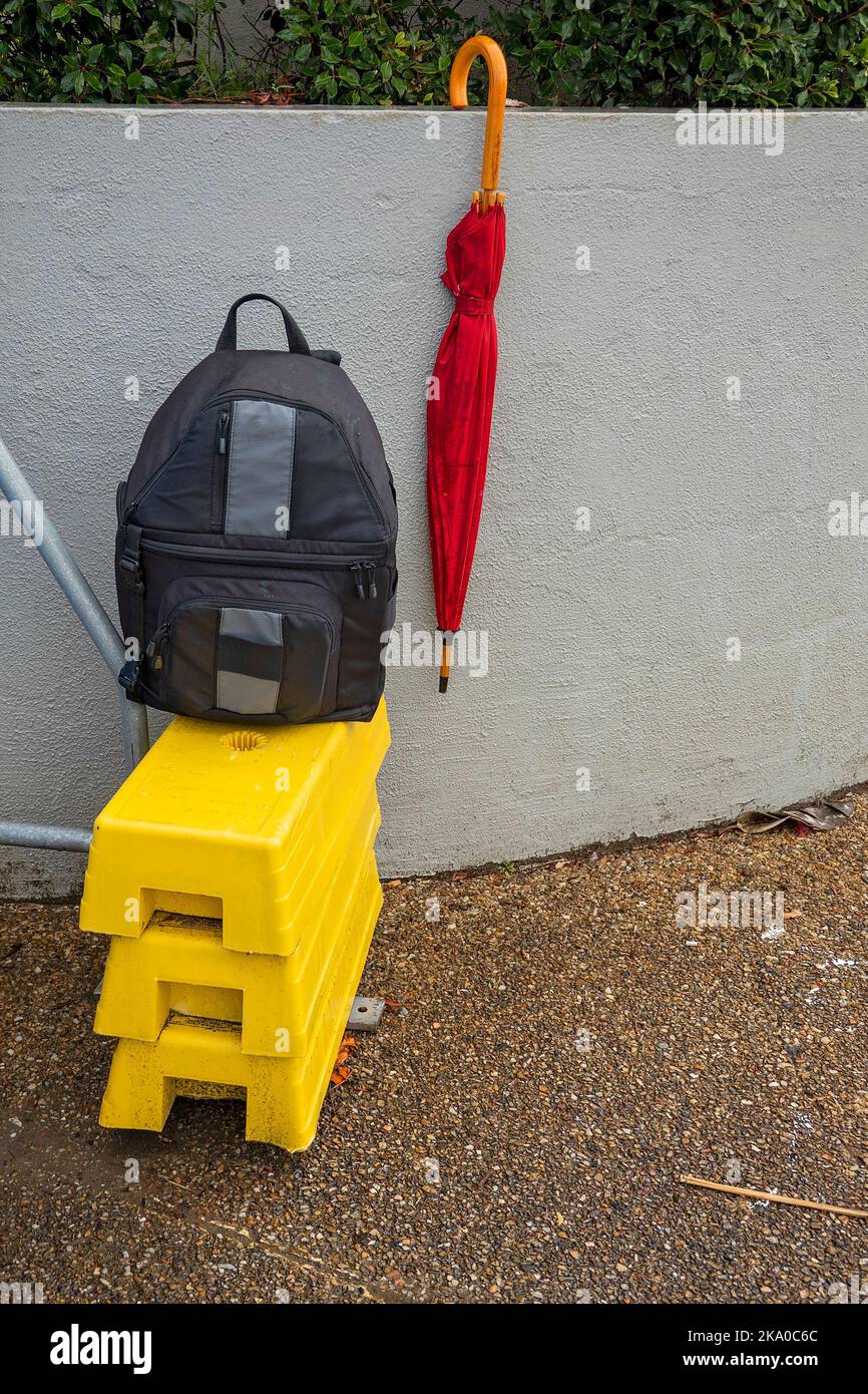 Camera bag and red umbrella on a yellow step stool against a grey wall ...