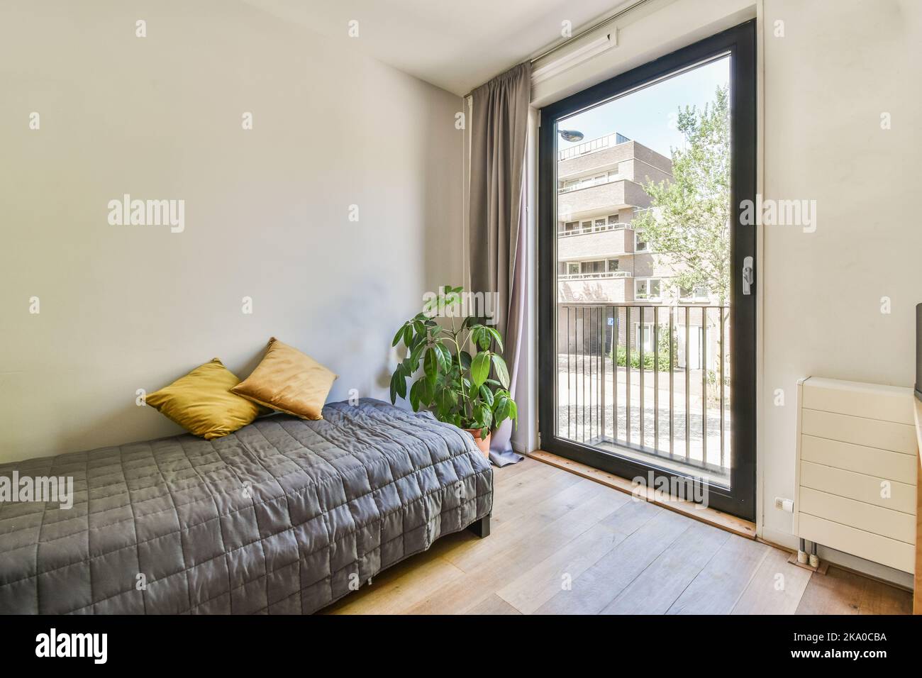 Comfortable bed located near balcony door with curtains in cozy light ...