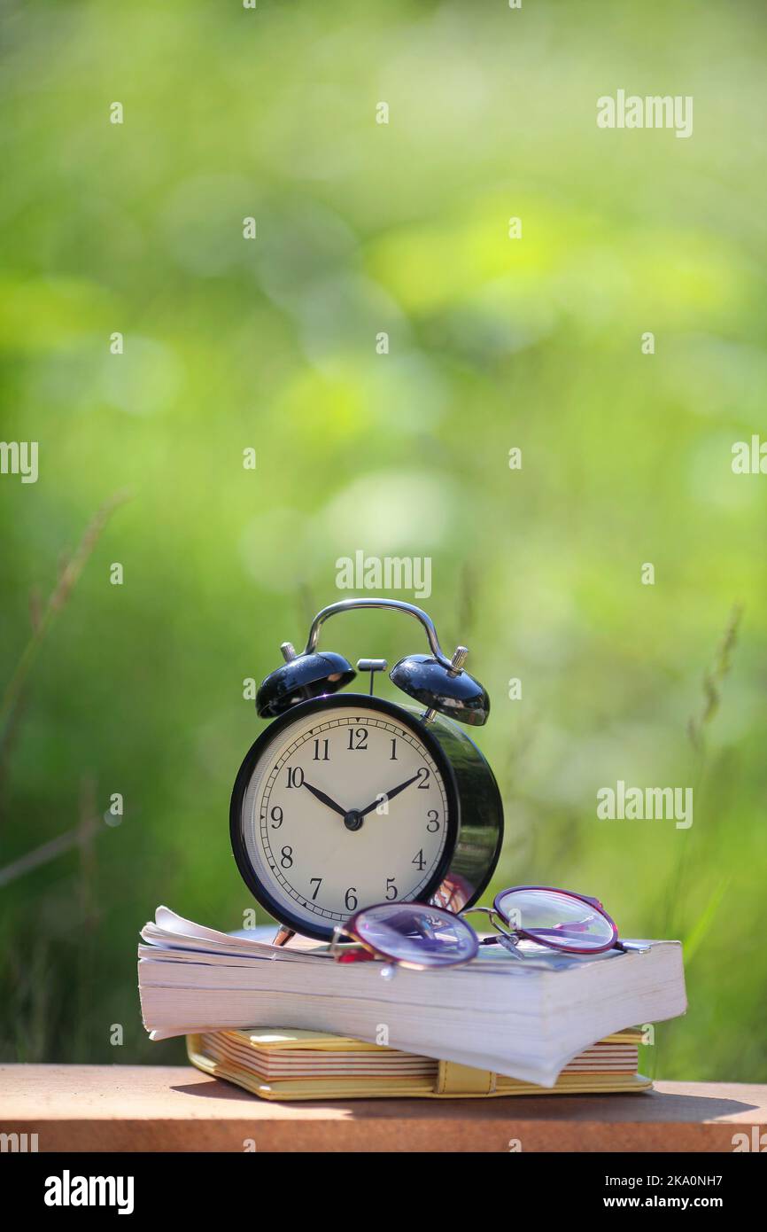 Black alarm clock stacked on organize book with nature bokeh background ...