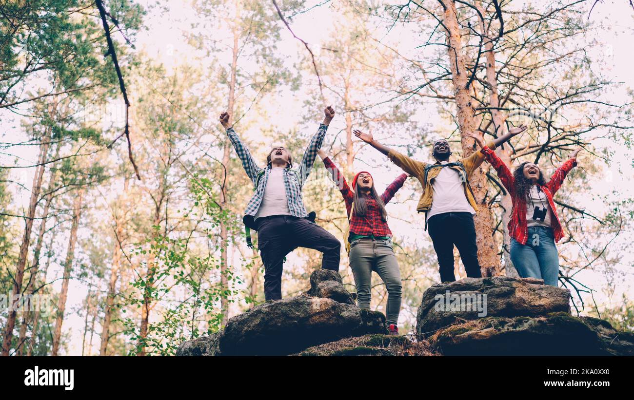 Low angle view of happy young people climbing up mountain raising hands ...