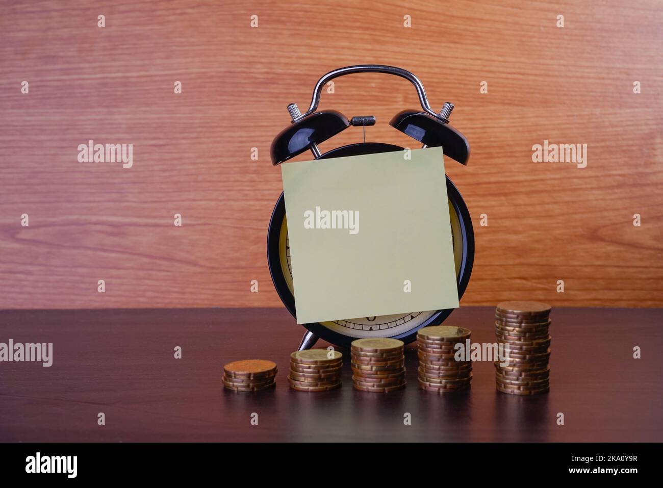 Yellow sticky note on black alarm clock and golden stacked coin Stock ...