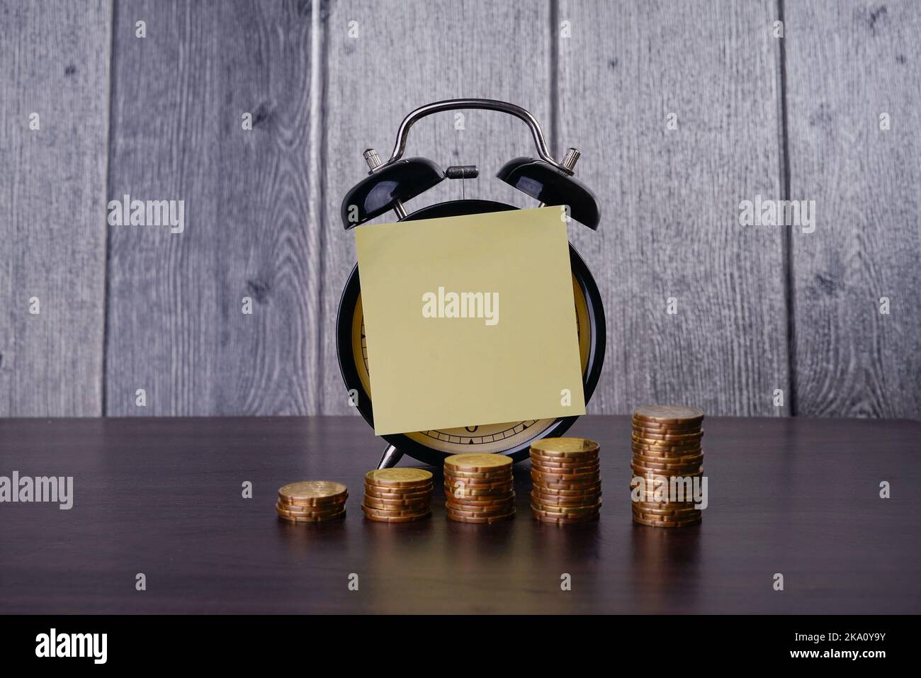 Yellow sticky note on black alarm clock and golden stacked coin Stock ...