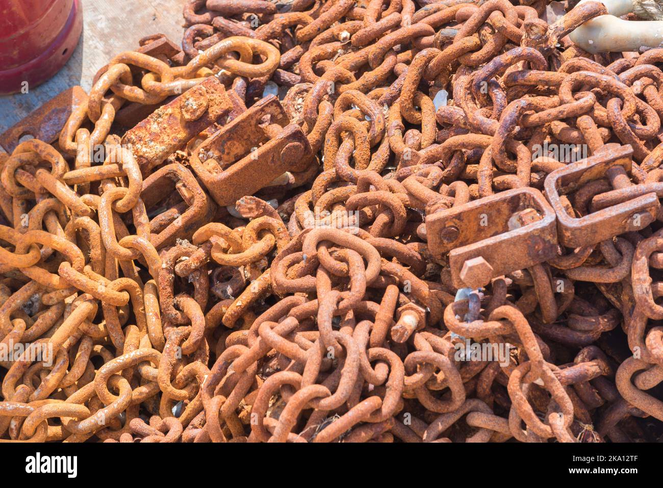 A huge length of orange coloured rusty boat chain lying in the sun in ...