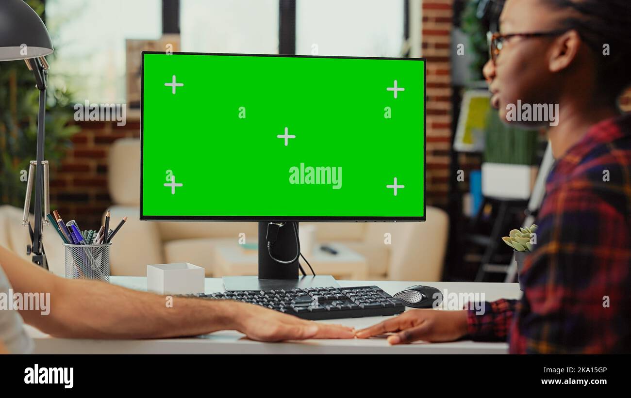 Multiethnic team working on computer with greenscreen at home, using monitor to examine isolated ...