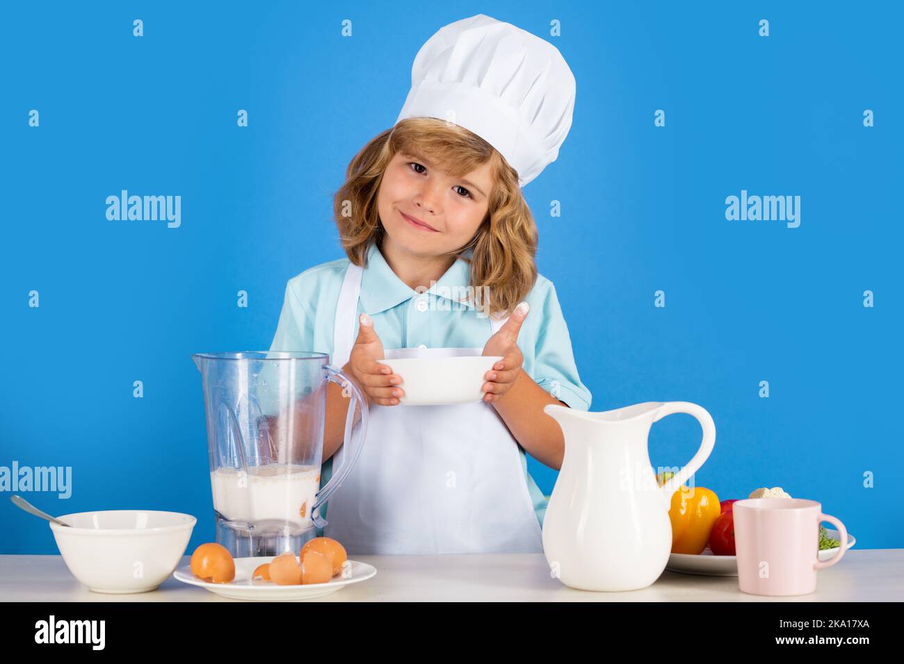 Child chef cook prepares food in isolated blue studio background. Kids ...