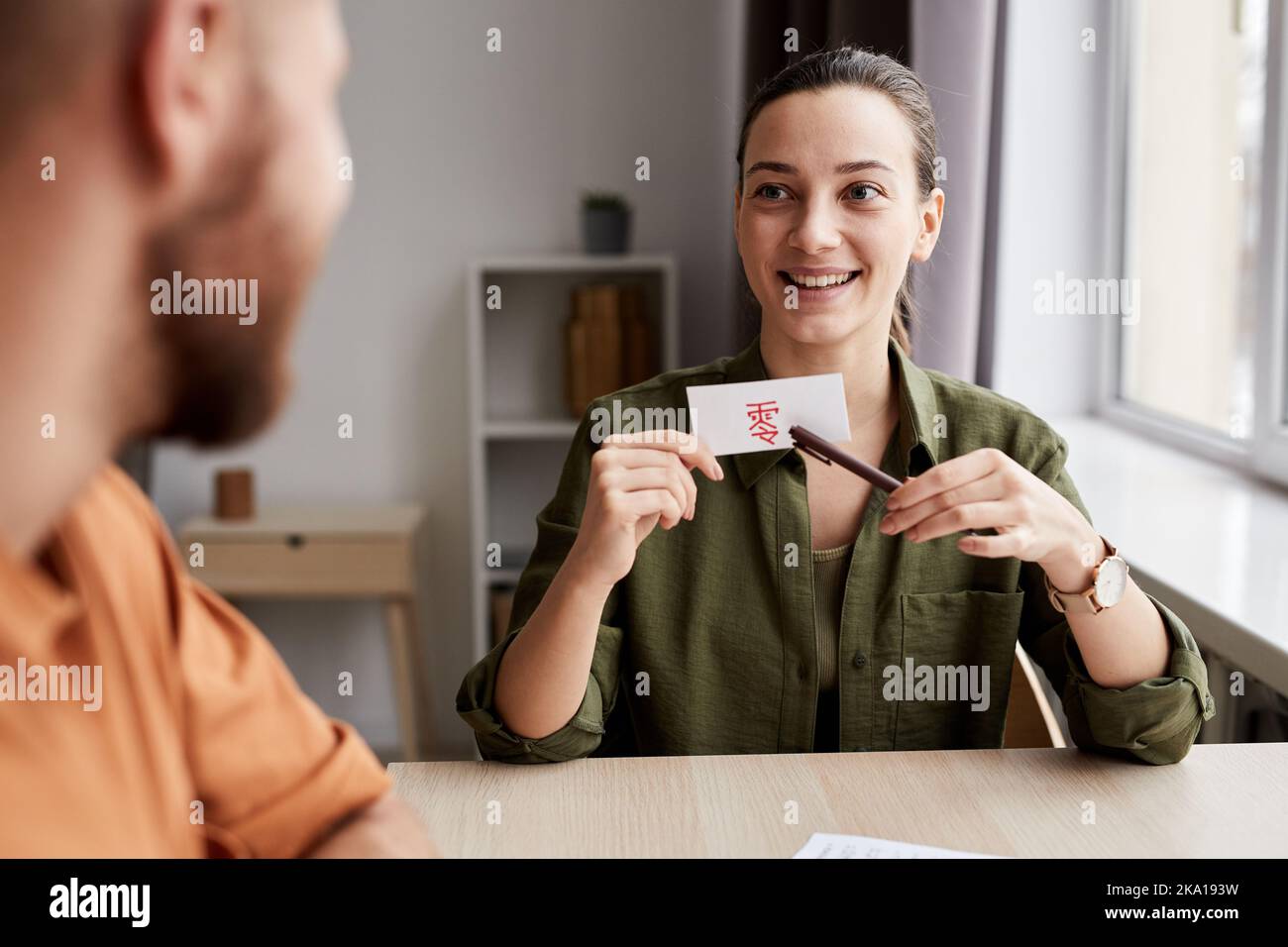 Young smiling female tutor pointing at paper card with Chinese ...
