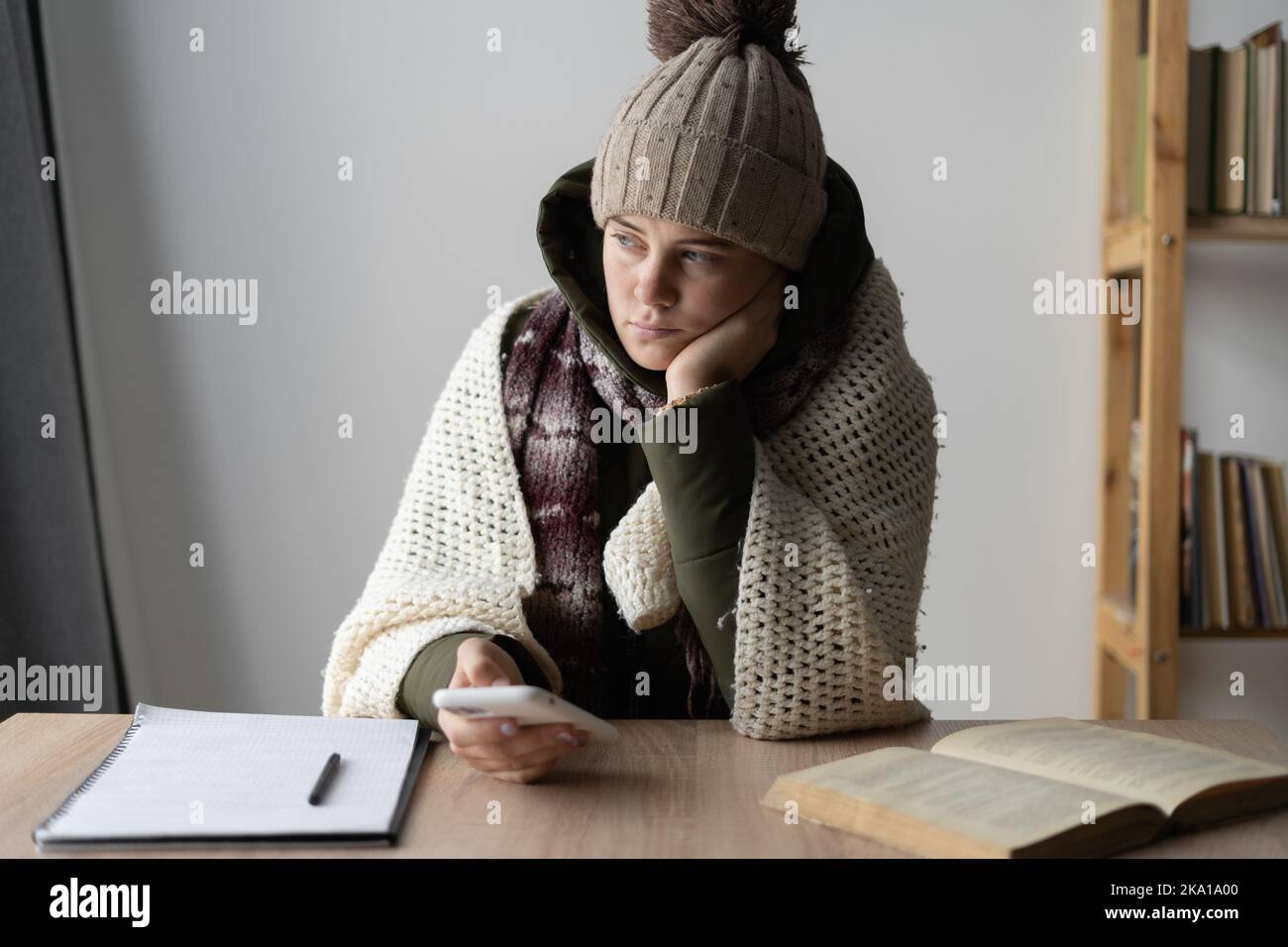 angry frozen woman warmly dressed in a cold house sitting at a table ...