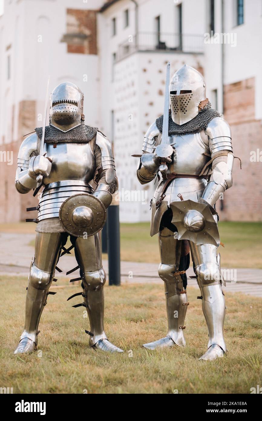 two knights in ancient metal armor stand at the stone wall of the ...