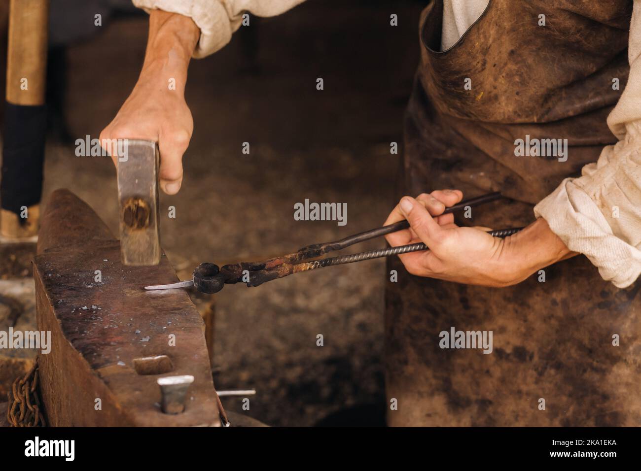 A blacksmith manually forges red-hot metal on an anvil with a hammer ...