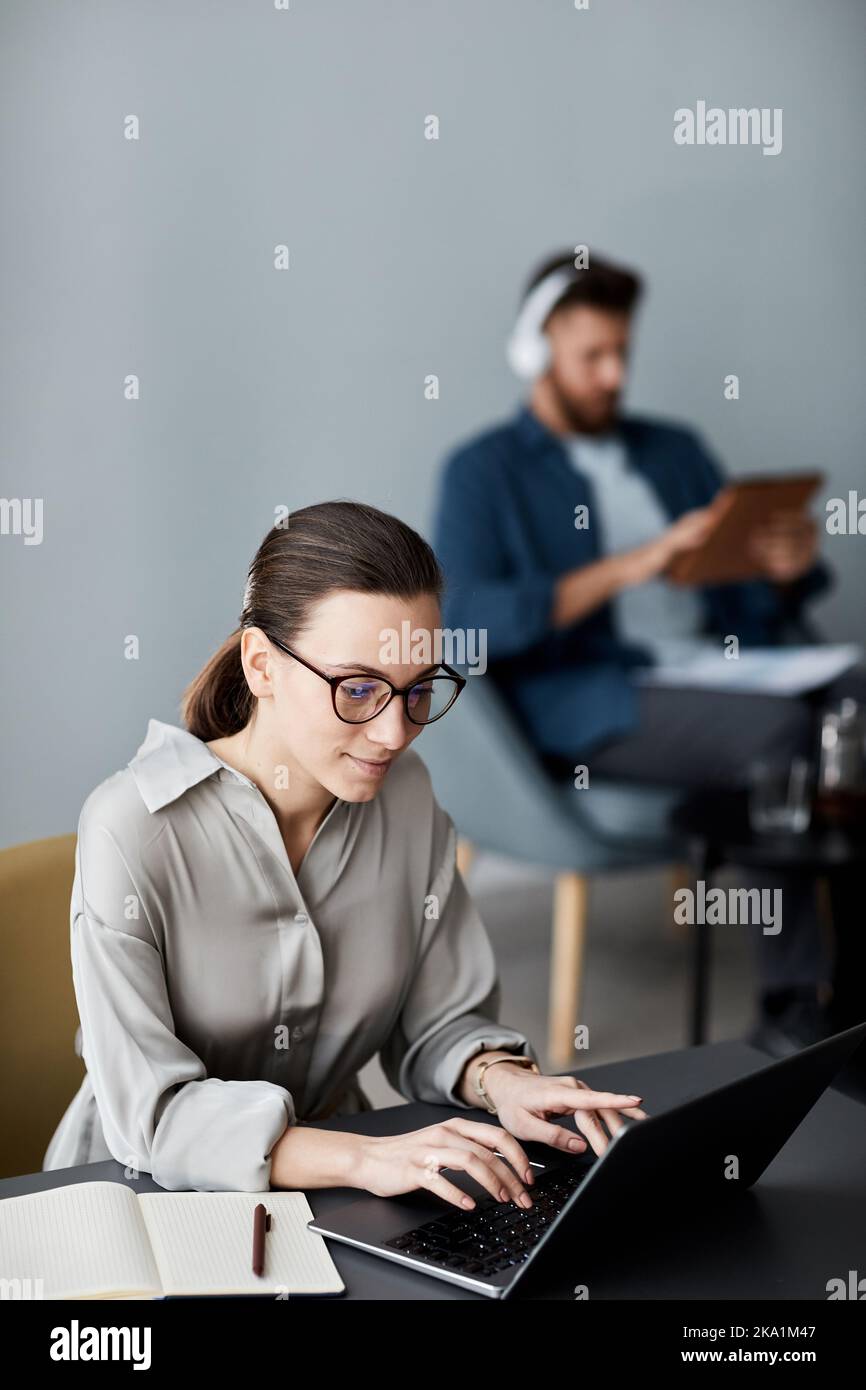 Young pretty student typing while sitting by desk in front of laptop ...