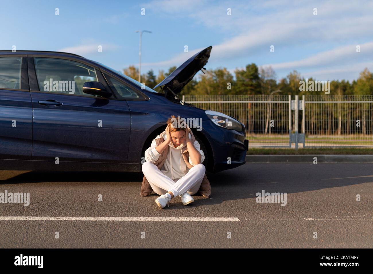 frustrated woman sits holding her head on the road next to a collapsed ...