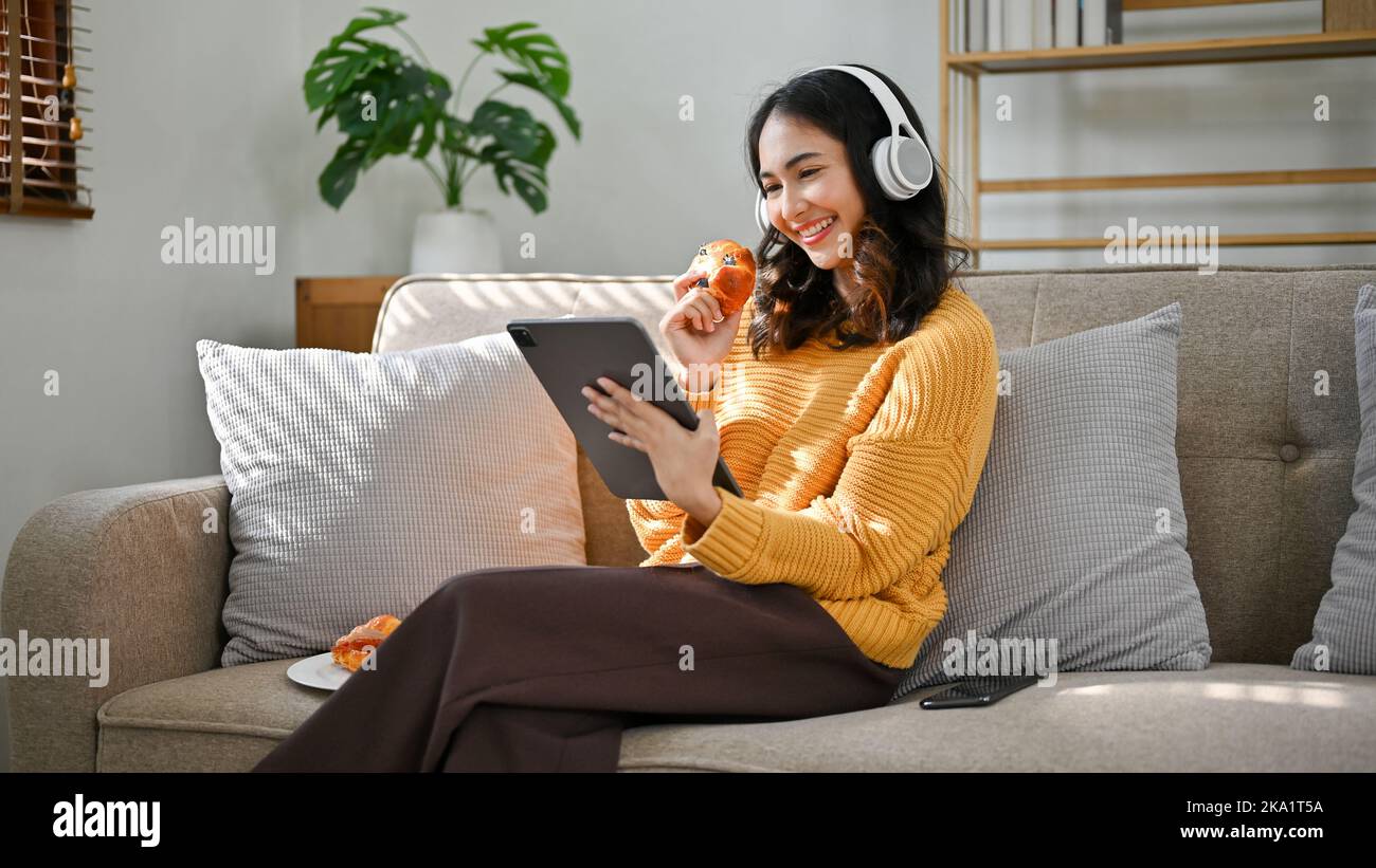 Charming young Asian female wearing headphones, watching something on ...