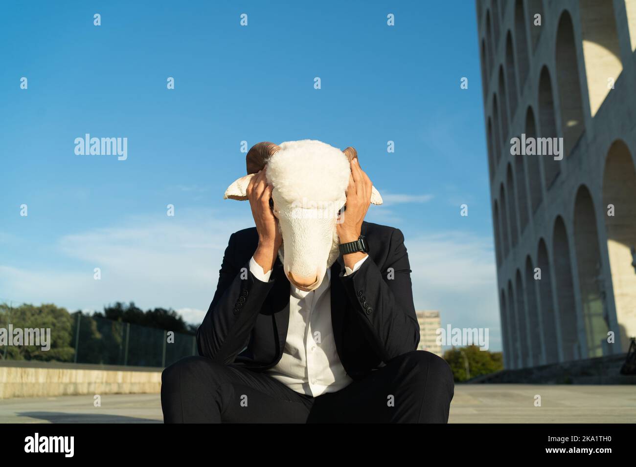 Sheep-headed businessman sitting on a ladder with his hands on his head ...