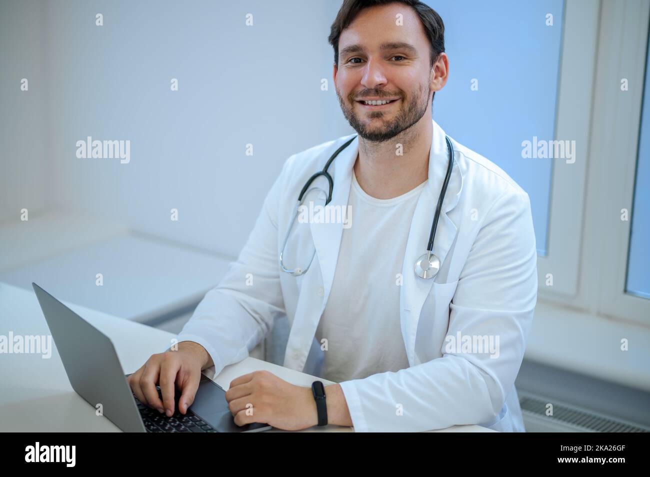 Dark-haired bearded young doctor at his working place in the hospital ...