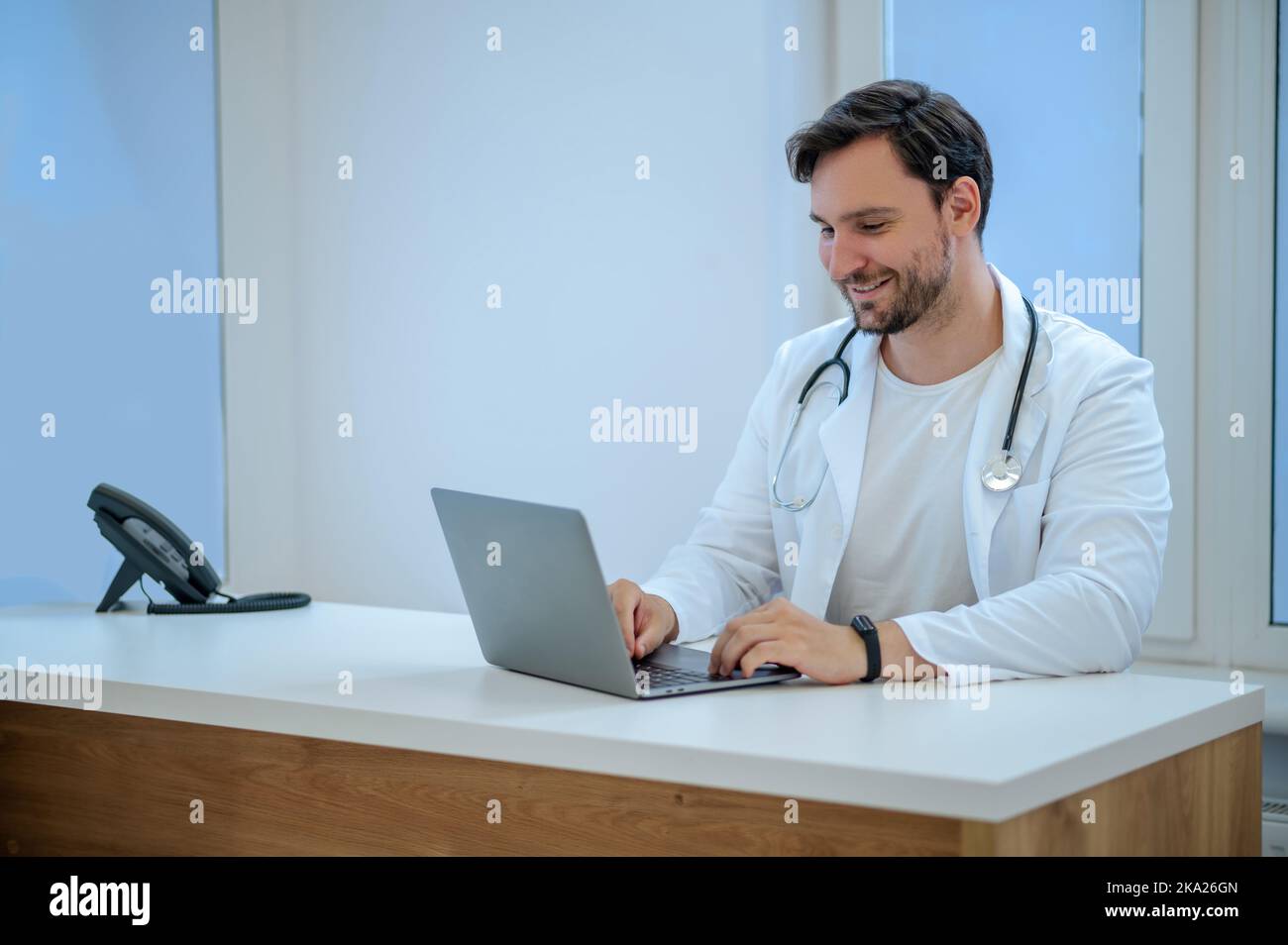 Dark-haired bearded young doctor at his working place in the hospital ...