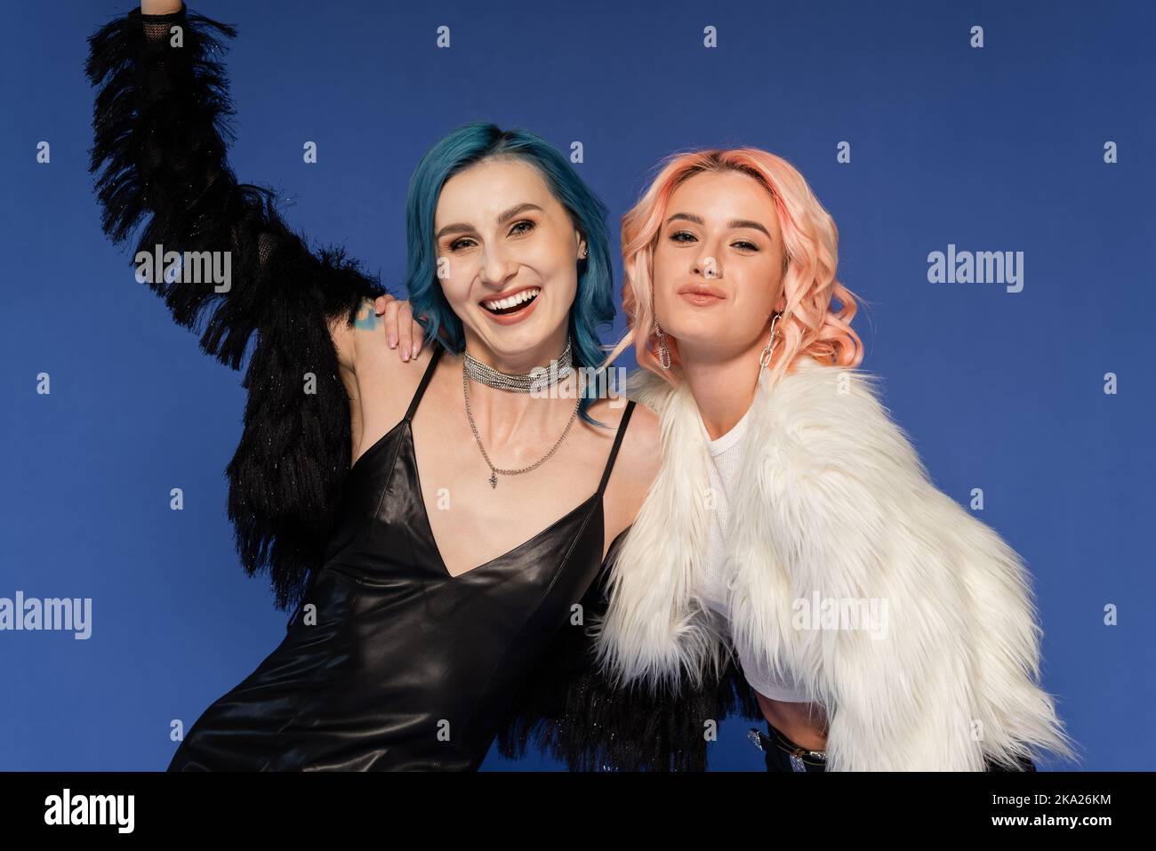 queer person hugging friend in black faux fur jacket posing with raised ...