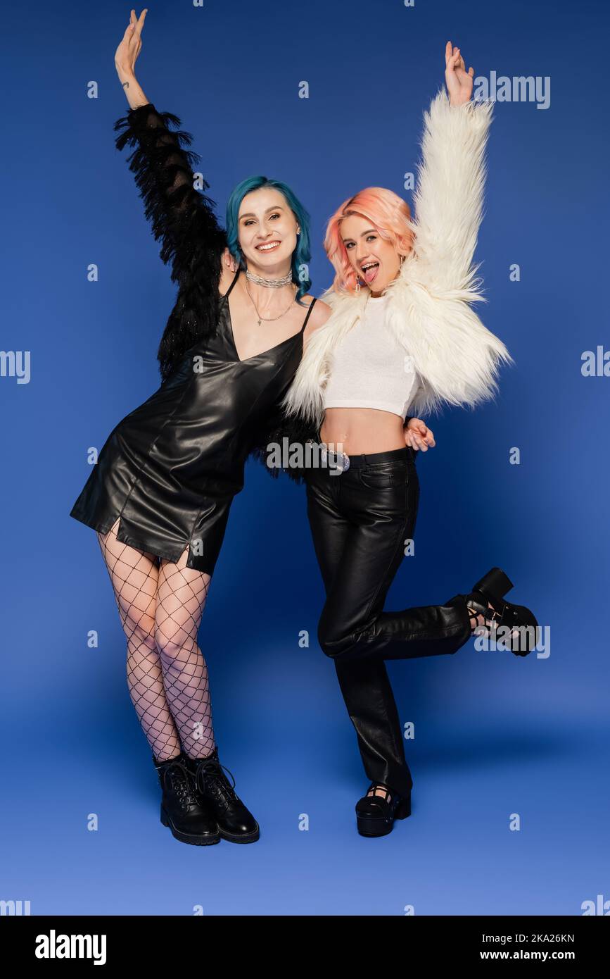 full length of nonbinary person sticking out tongue while posing with happy friend on blue ...