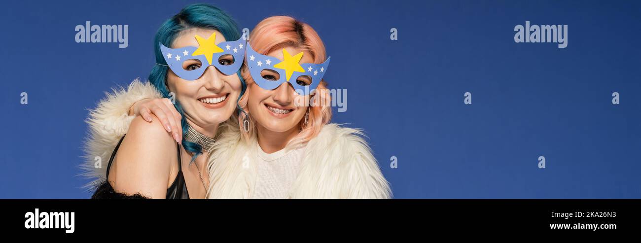 happy nonbinary friends in party masks hugging isolated on blue, banner ...