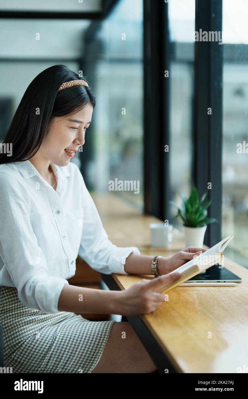 Portrait of a beautiful Asian female employee reading a book during her ...