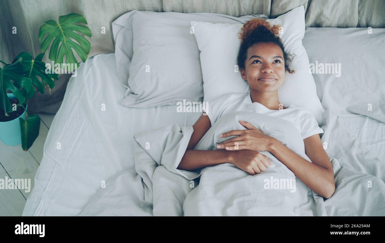 Happy young woman is lying in bed awake and smiling enjoying carefree ...