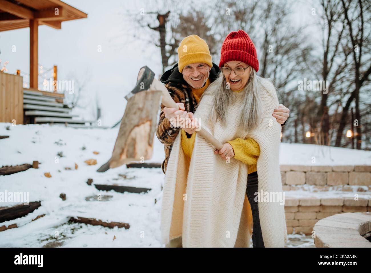 Senior couple chopping wood together in front of their house, during ...