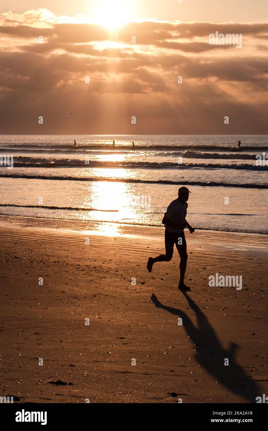 A vertical silhouette of people on a sandy beach at sunset in ...
