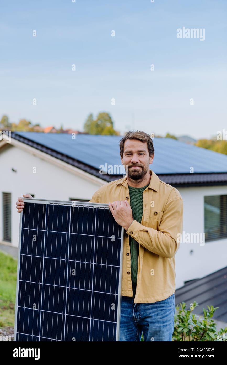 Mature man holding solar panel near his house with solar panels on the ...
