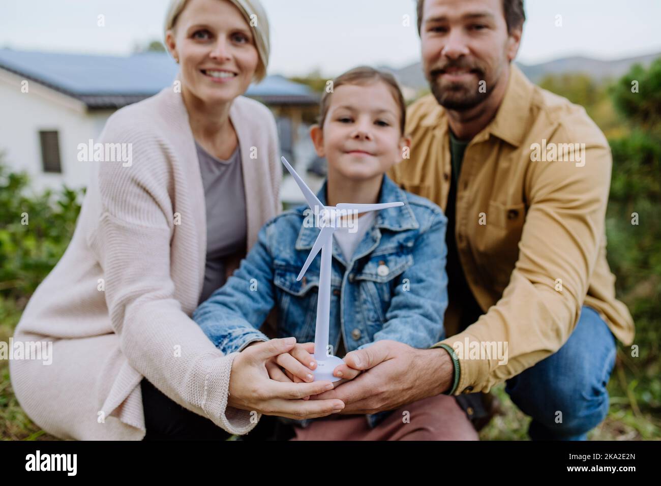 Happy family holding plastic model of wind turbine. Alternative energy ...