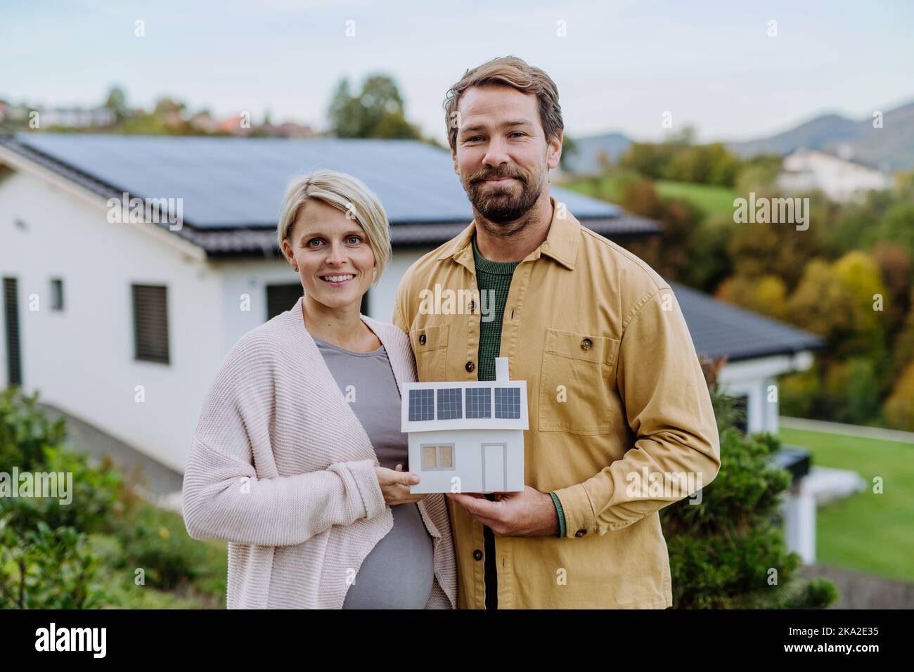 Close up of happy couple holding paper model of house with solar panels ...