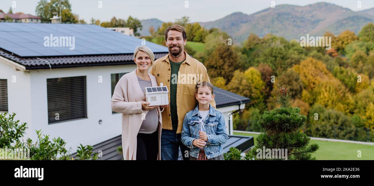 Happy family holding paper model of house with solar panels.Alternative ...