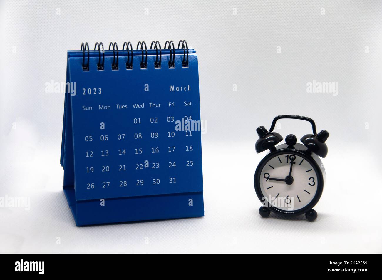 Alarm clock pointing at 9 o'clock with March 2023 calendar on white ...