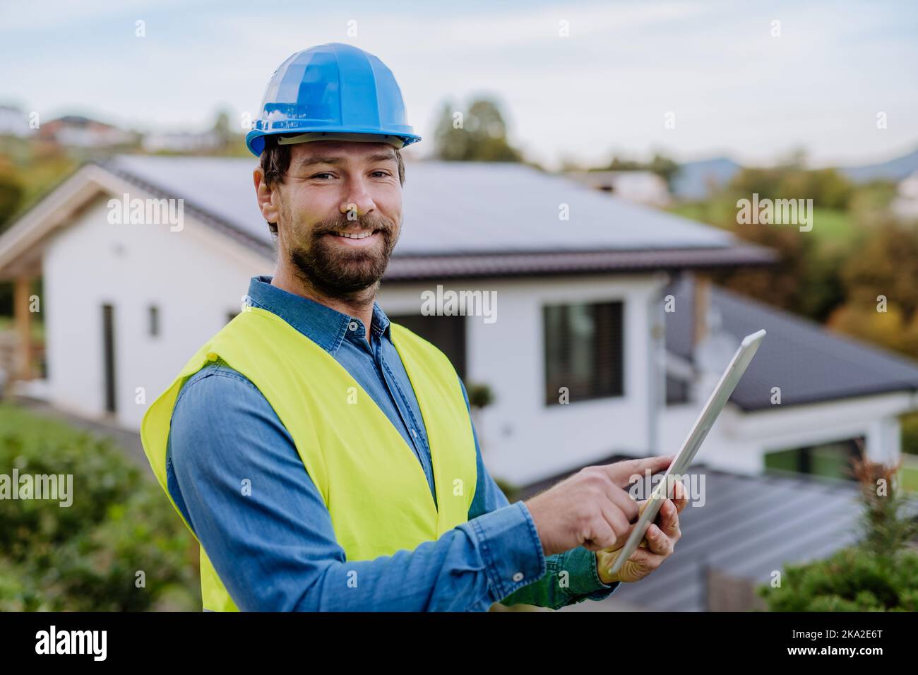Smiling handyman solar installer standying in front of family house ...