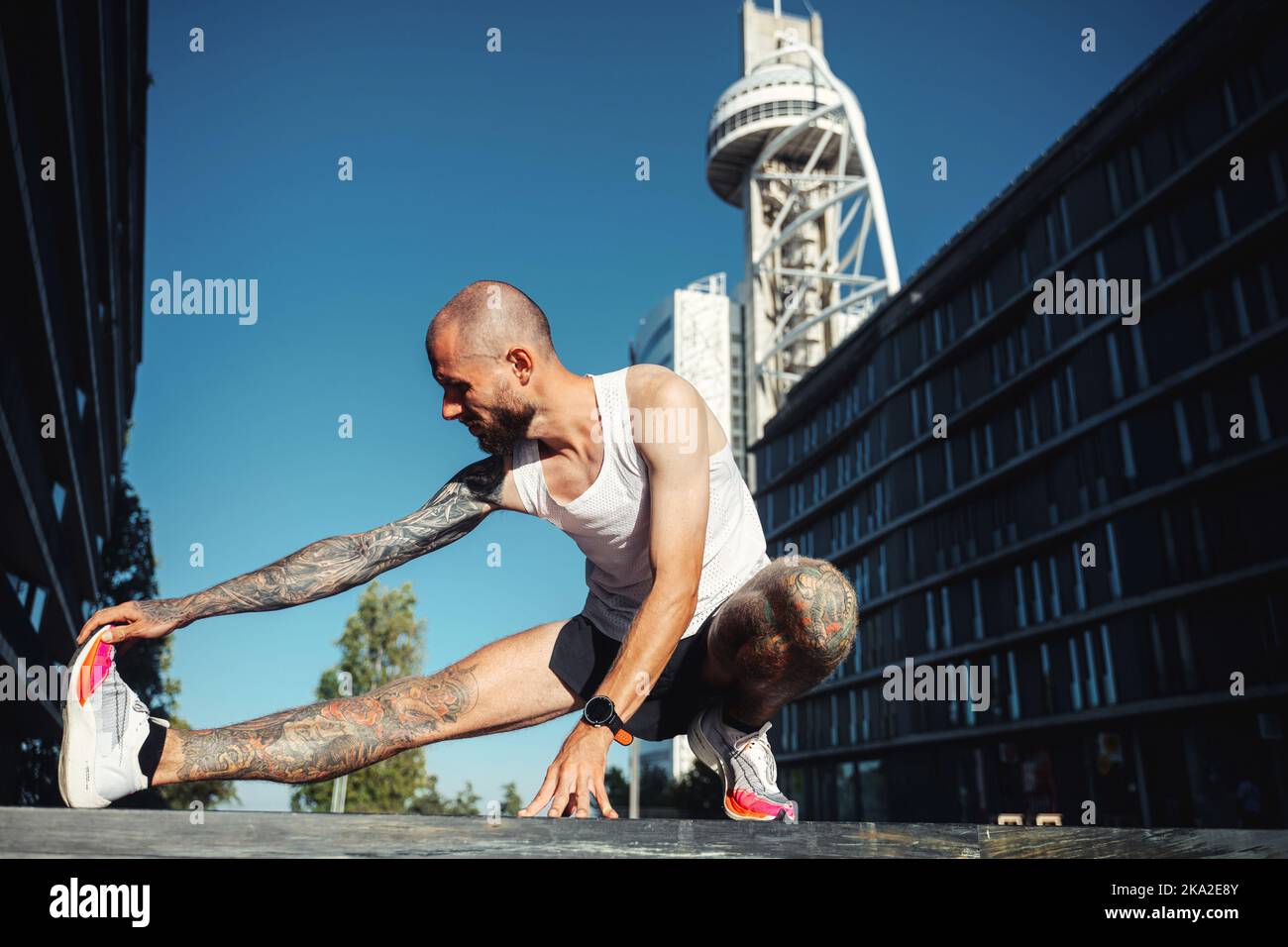 Young muscular tattooed man doing exercises, stretching early in the morning, bald bearded guy ...