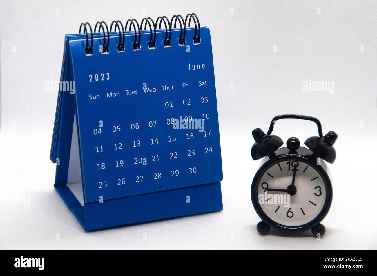 Alarm clock pointing at 9 o'clock with June 2023 calendar on white ... Alarm clock pointing at 9 o'clock with June 2023 calendar on white ...